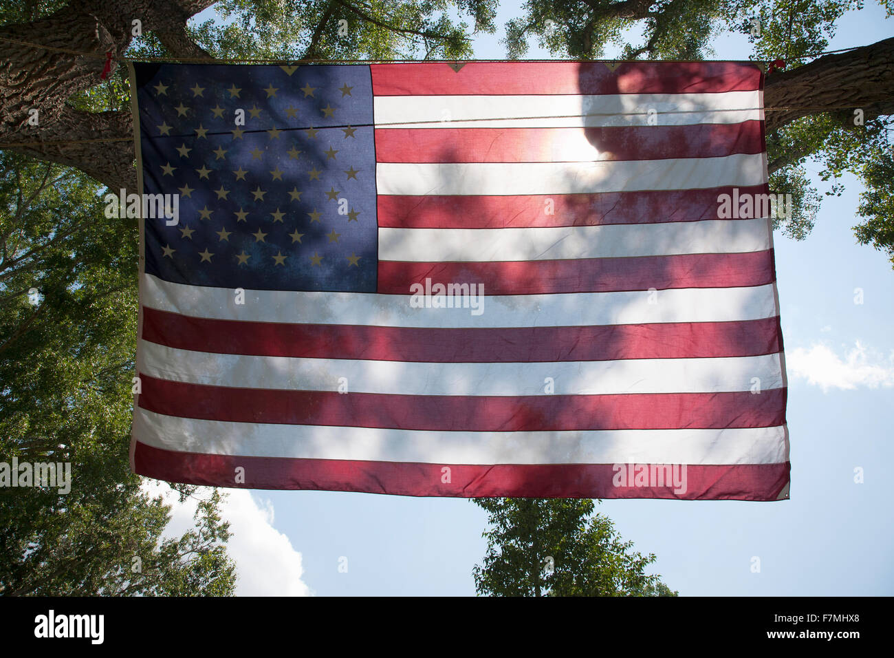 Sun and clouds are seen through backlighted American Flag, Ridgeway, CO ...