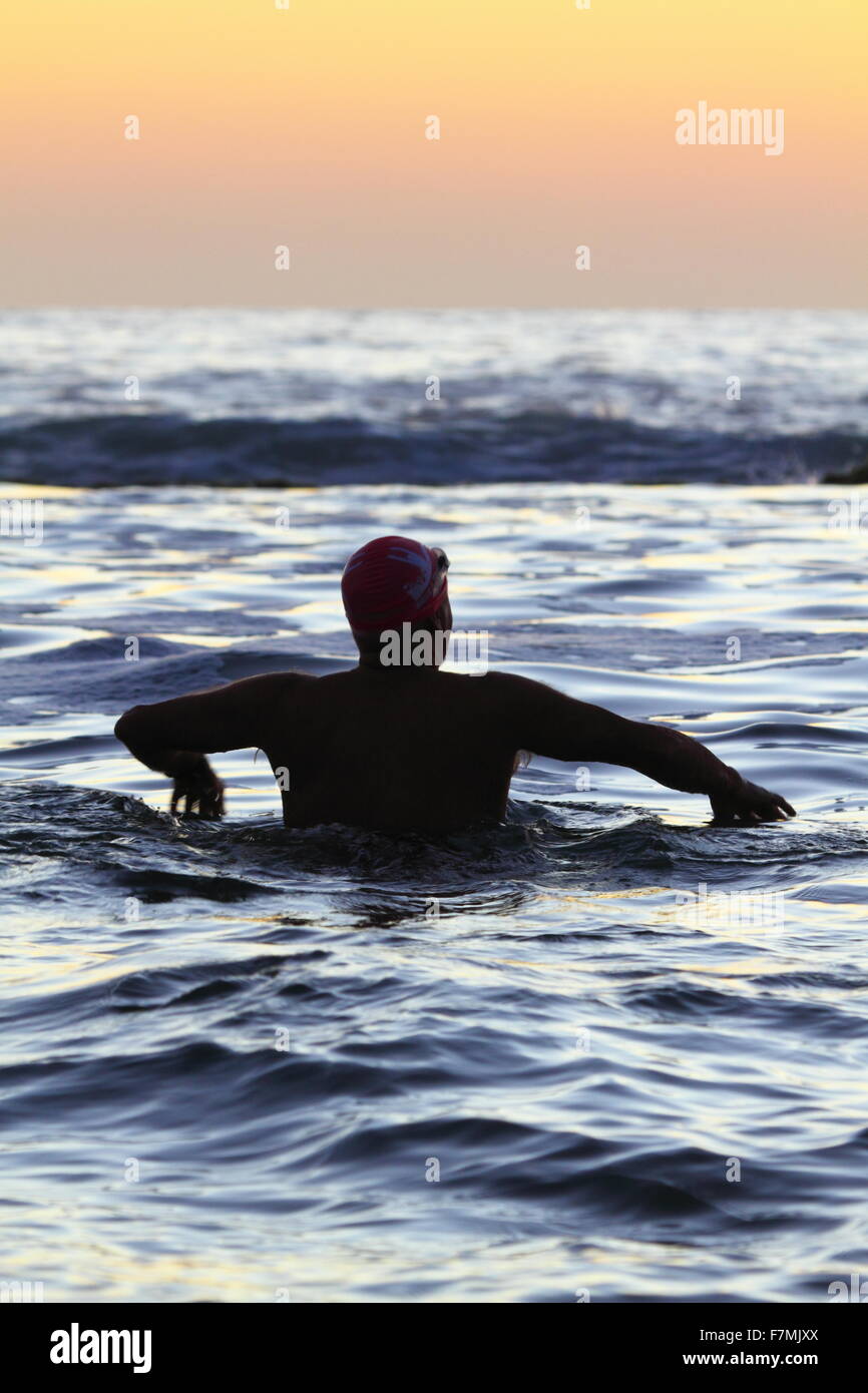 A male swimmer wading out to swim laps and exerce in an ocean rock pool ...