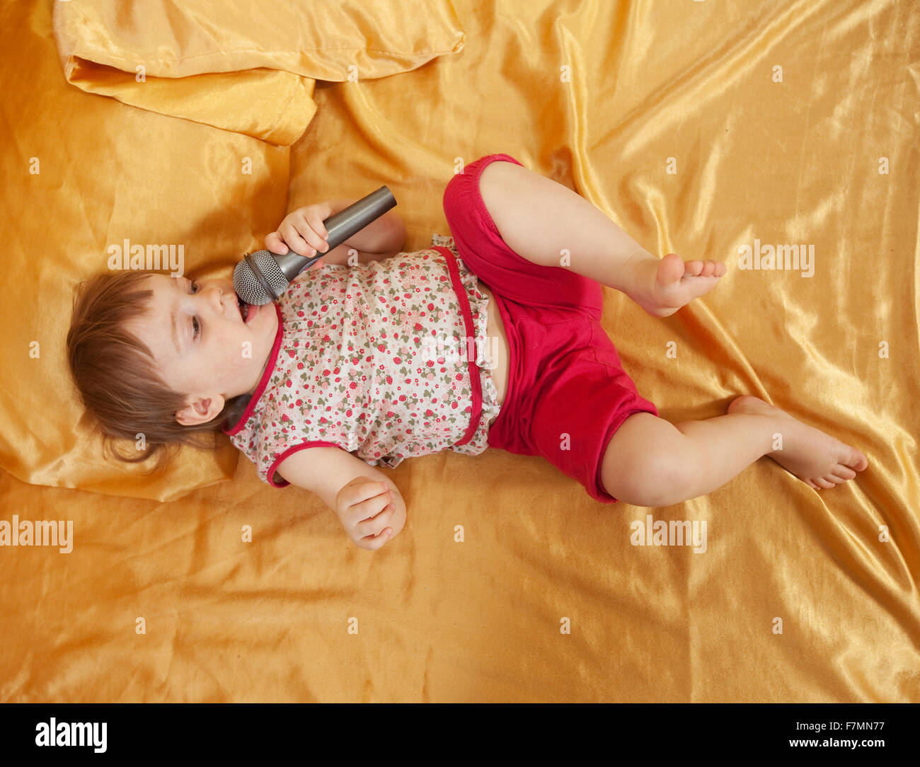 Toddler sings into a microphone lying on the bed Stock Photo - Alamy