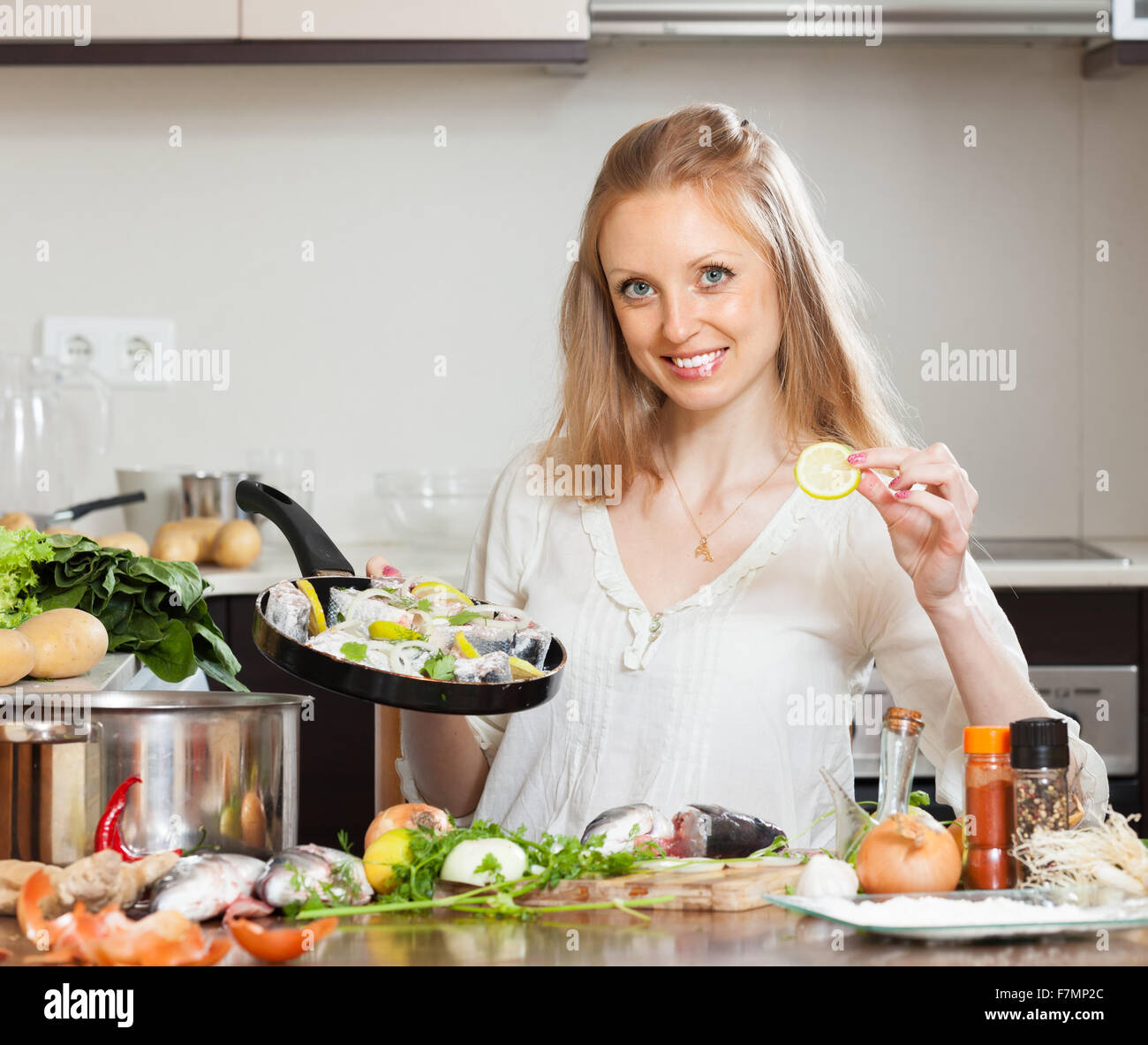 Smiling girl cooking fish with lemon in frying pan at kitchen Stock ...
