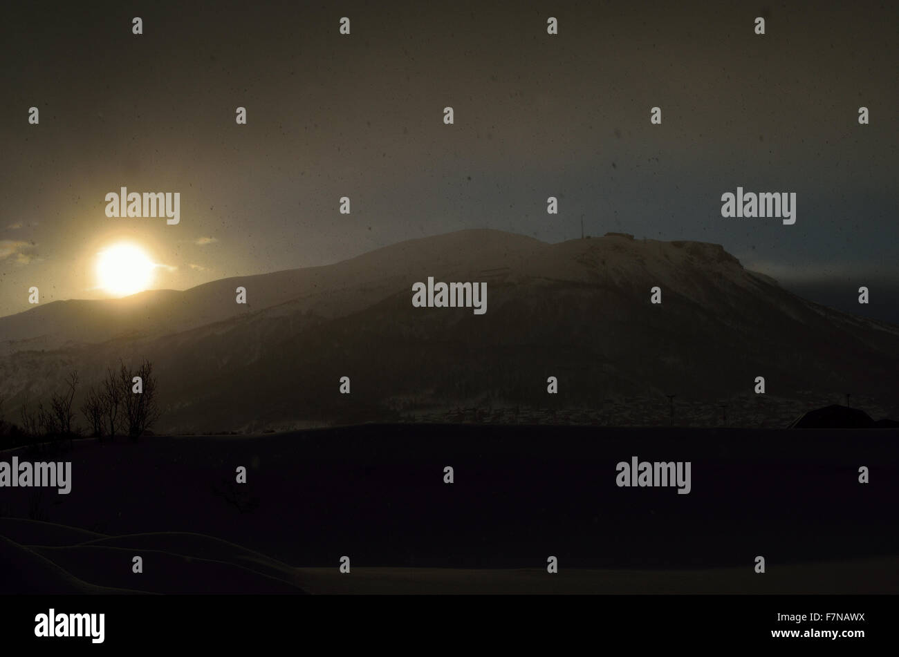 sun between clouds over snowy mountain as the snow is falling down ...