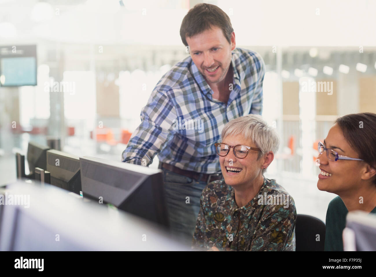 Smiling students at computer in adult education classroom Stock Photo ...