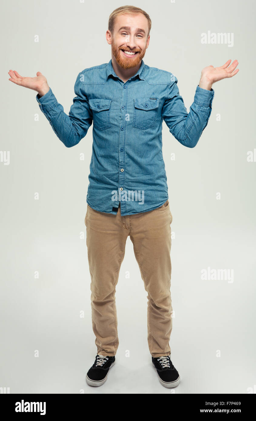Full length portrait of a smiling casual man shrugging shoulders ...