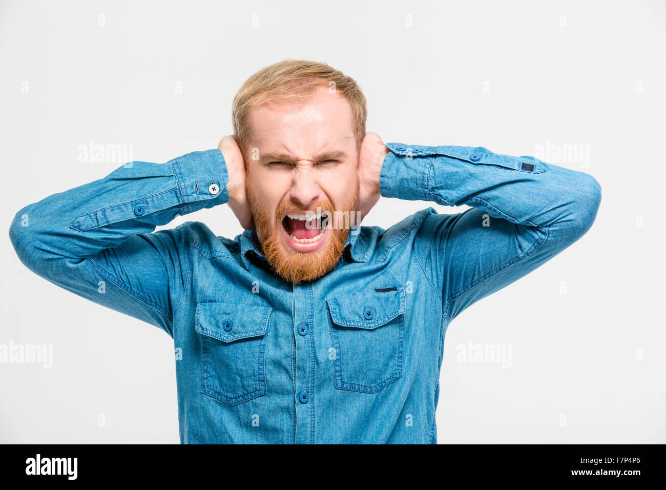 Mad hysterical young man with beard closed ears by hands and screaming ...