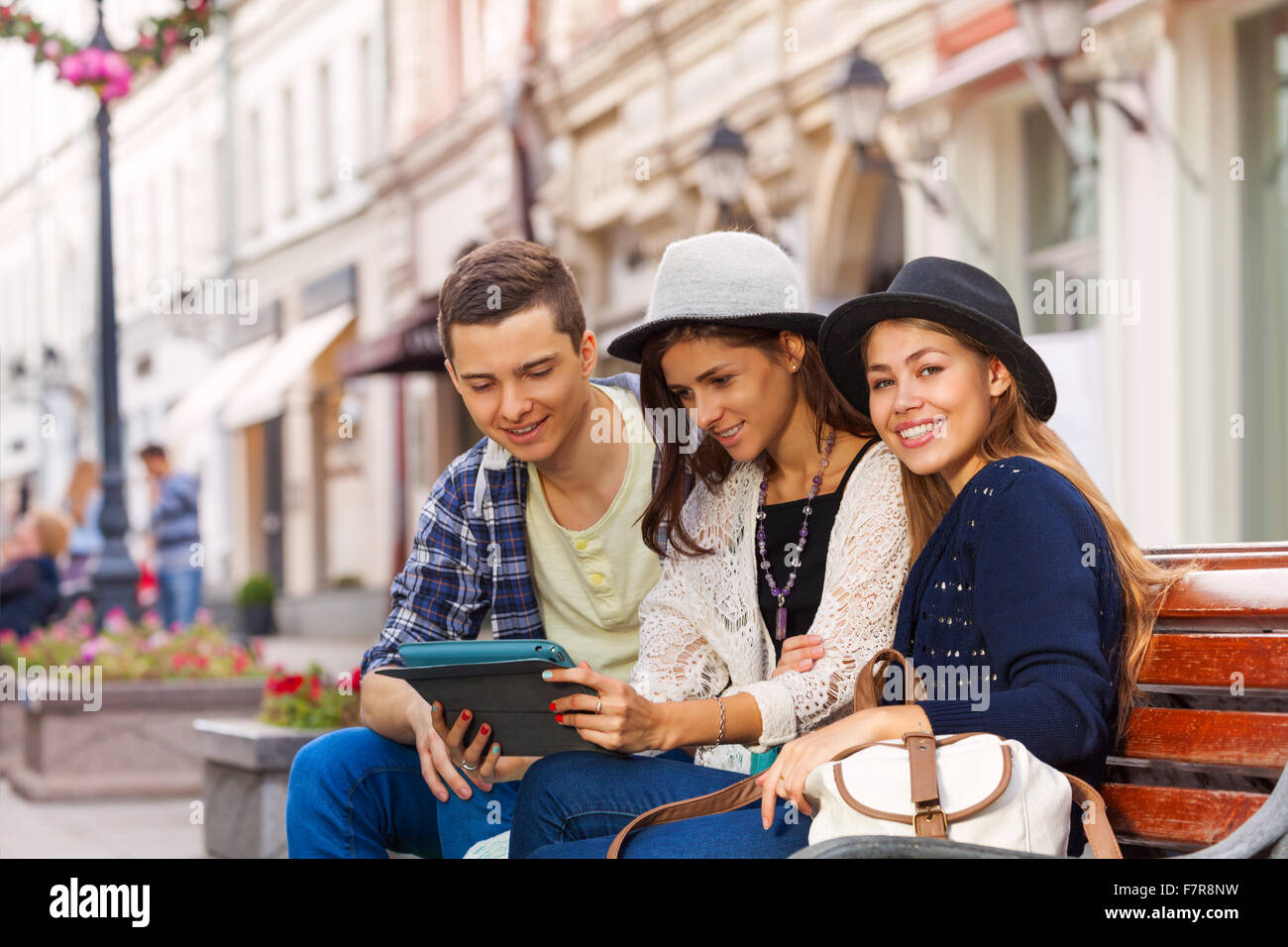 Three friends sit together with tablet on bench Stock Photo - Alamy
