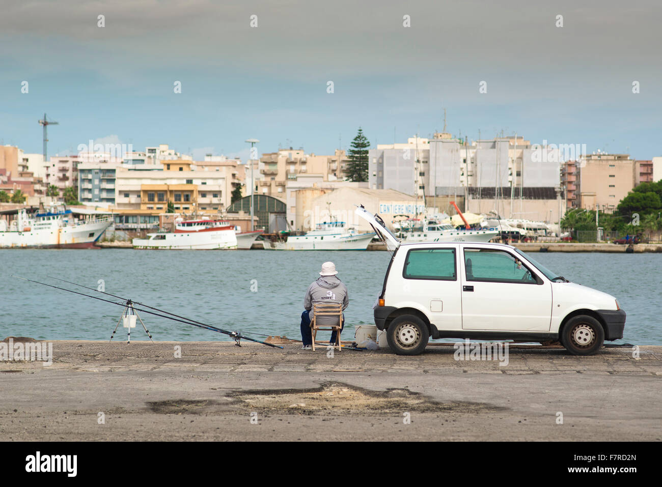 Man fishing alone, rear view of a man fishing from the quay in the port ...