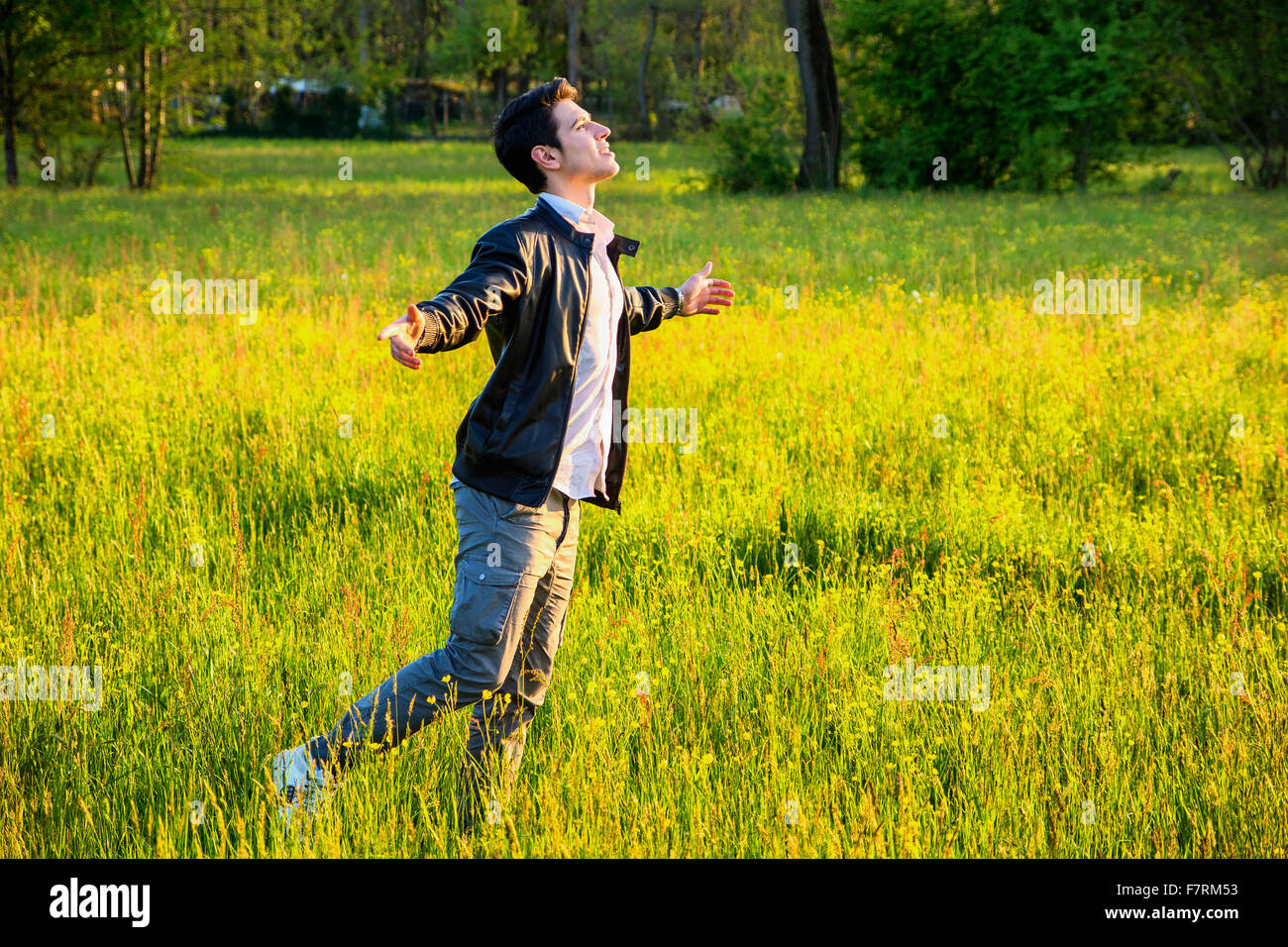Young man celebrating nature standing in grassland with outstretched ...