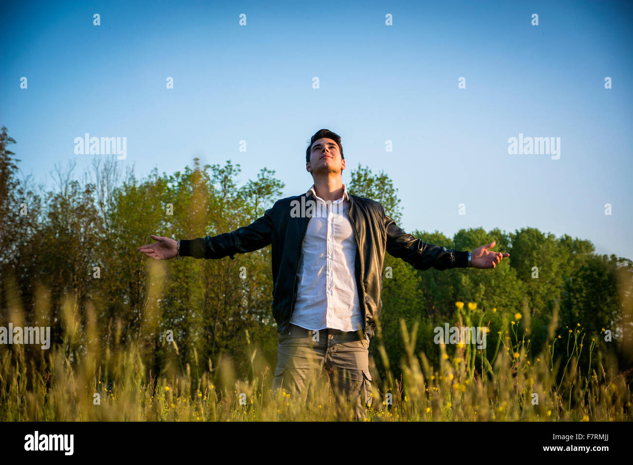 Young man celebrating nature standing in grassland with outstretched ...