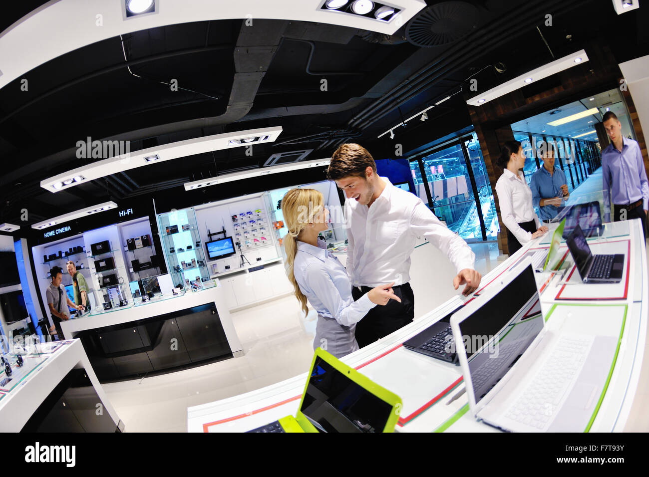 people in consumer electronics retail store looking at latest laptop ...