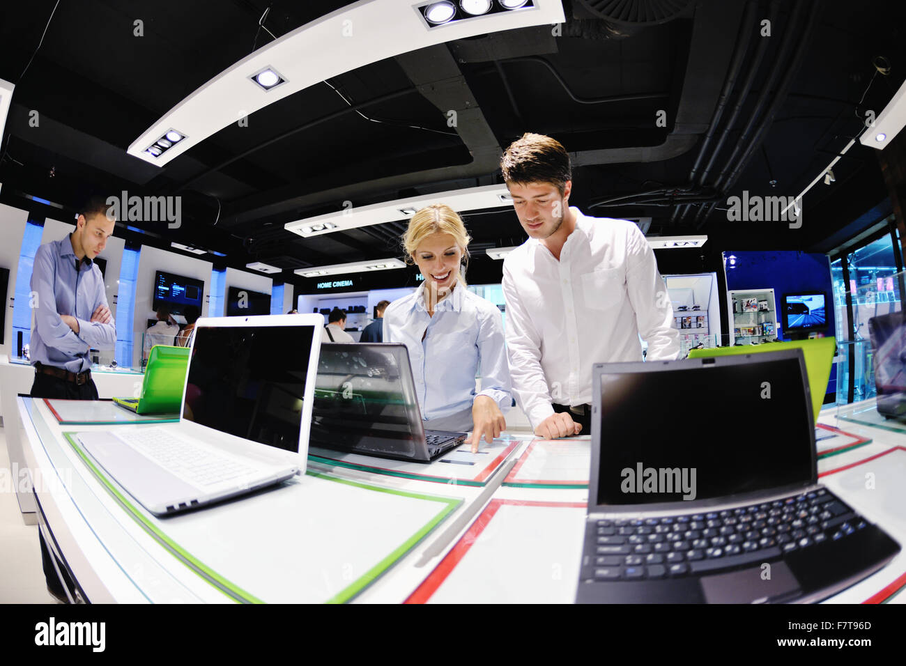people in consumer electronics retail store looking at latest laptop ...