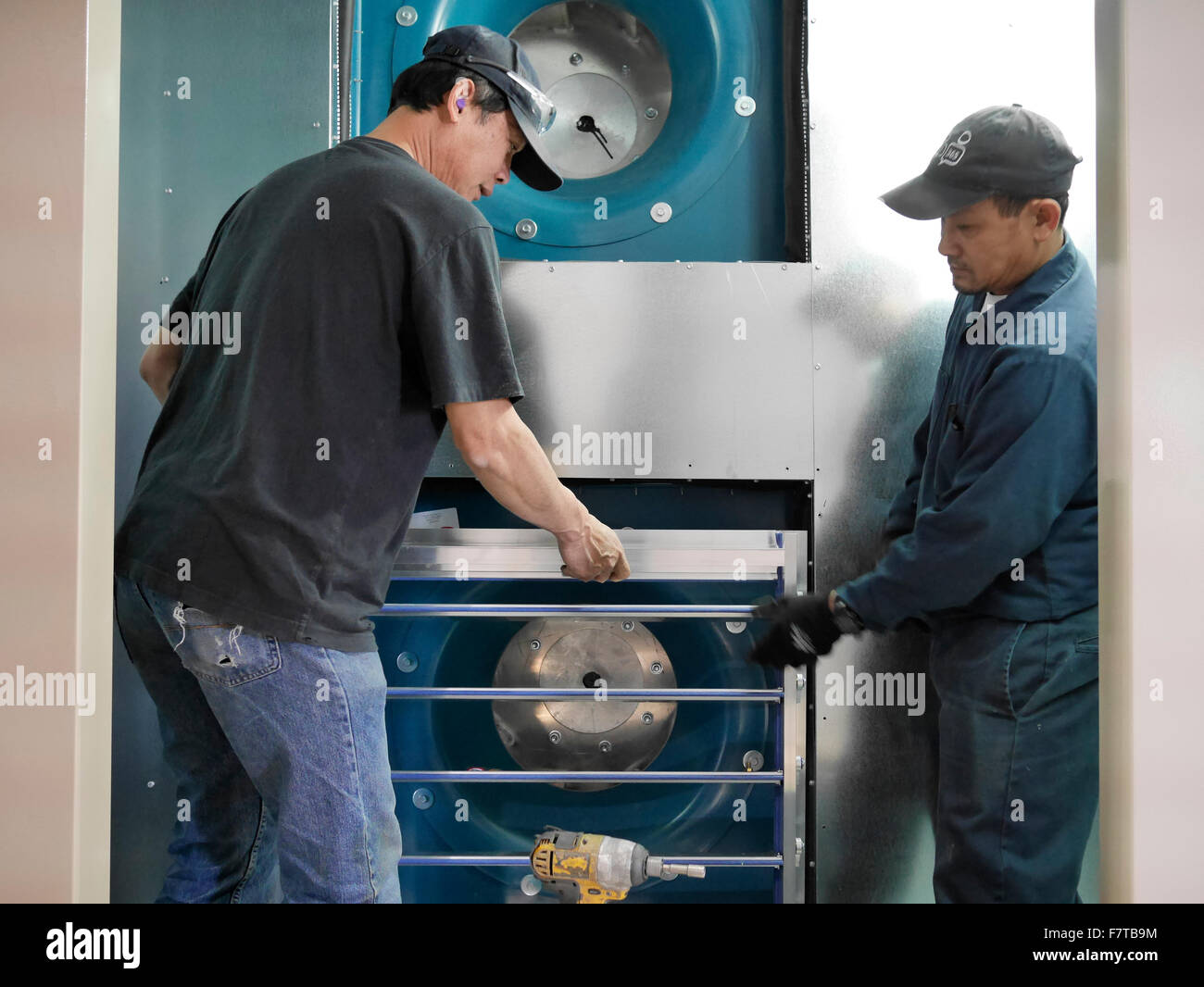 Two workers fixing metal grid in HVAC fan unit Stock Photo - Alamy
