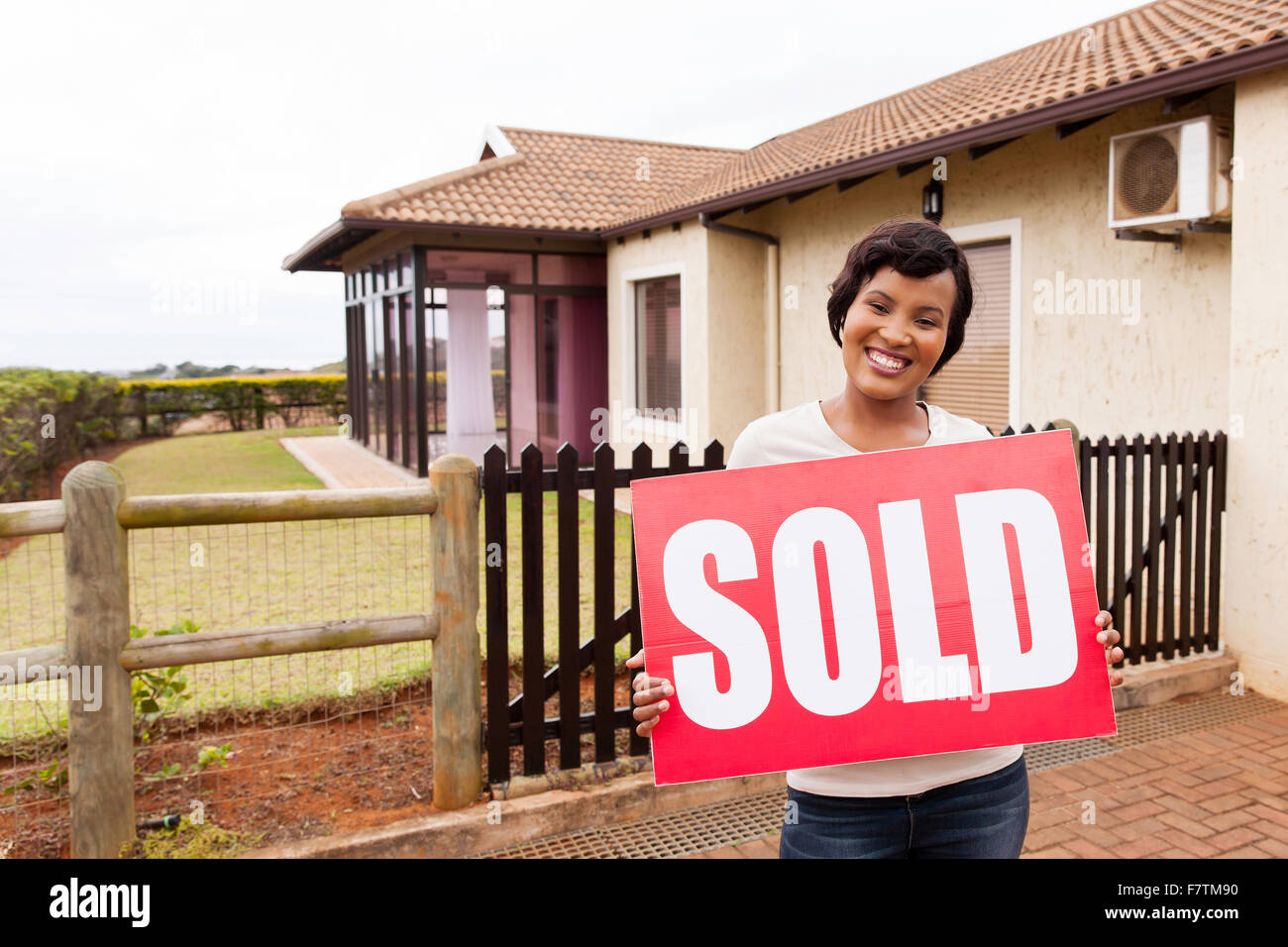 happy African woman holding sold sign in front of house Stock Photo - Alamy
