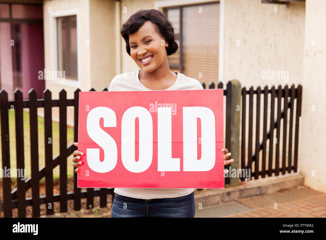 cheerful African American woman holding sold sign outside her house ...