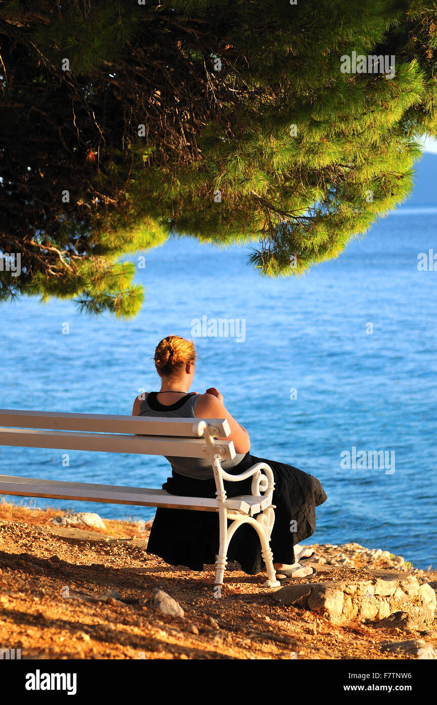 Single woman sitting alone by the beach watching sunset Stock Photo - Alamy