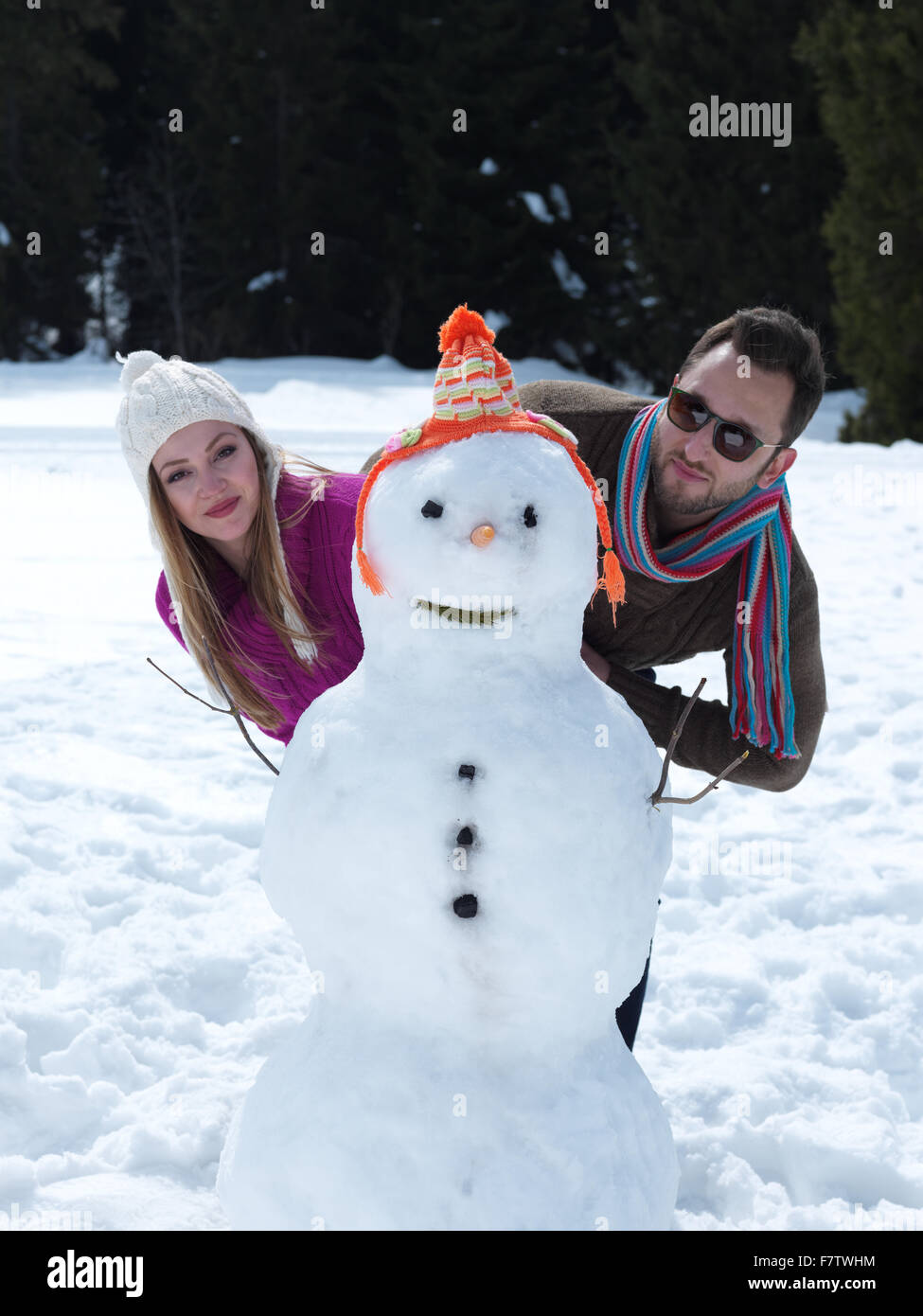portrait of happy young couple with snowman at beautiful winter day ...