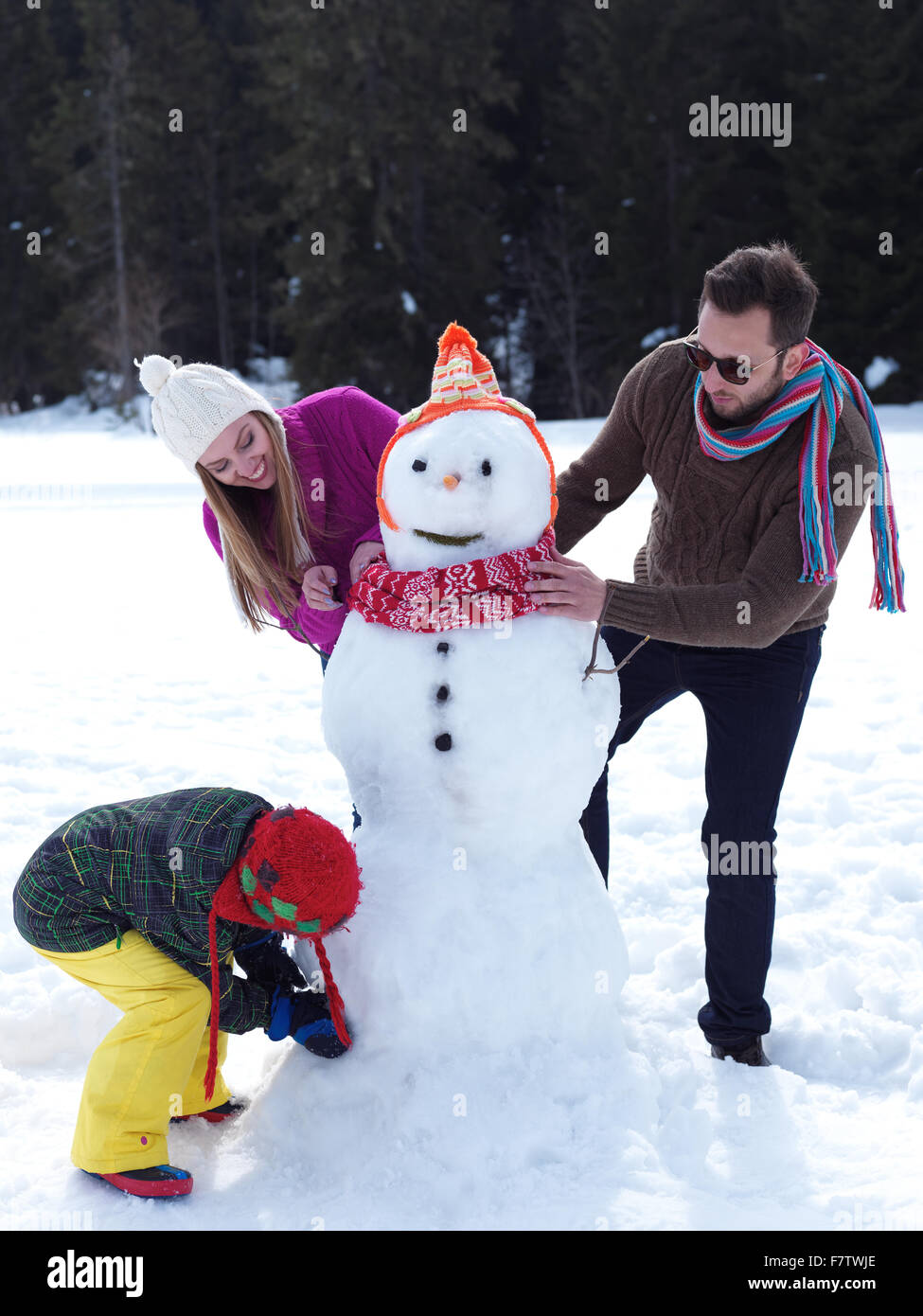 happy young family playing in fresh snow and making snowman at ...