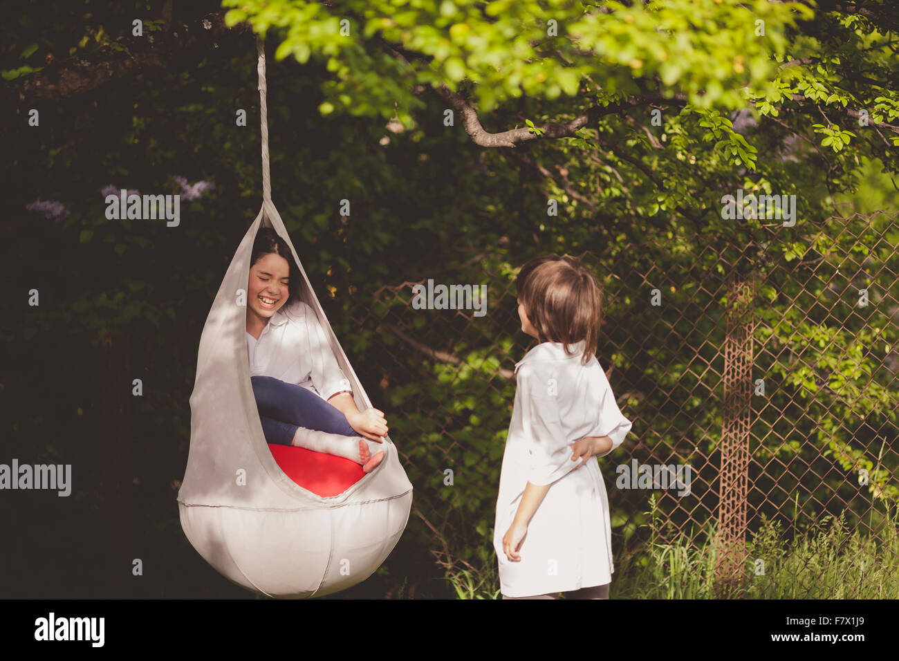 Girl sitting in a hanging chair talking to a boy Stock Photo - Alamy