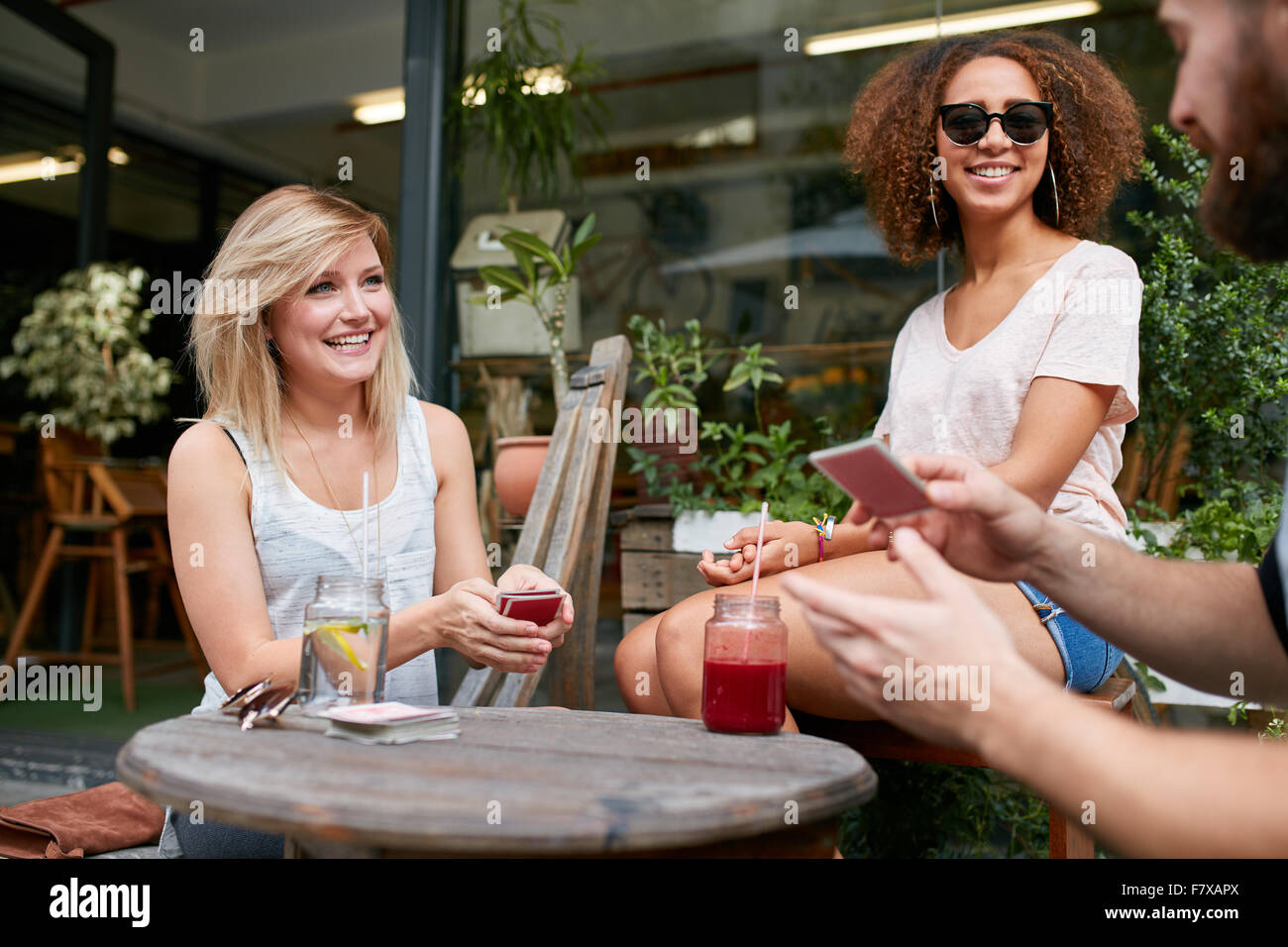 Happy young people playing cards at outdoor coffee shop. Three friends ...