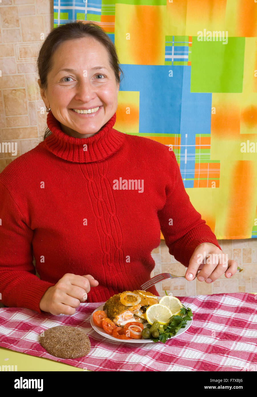 mature woman eating breaded fish in her kitchen Stock Photo - Alamy