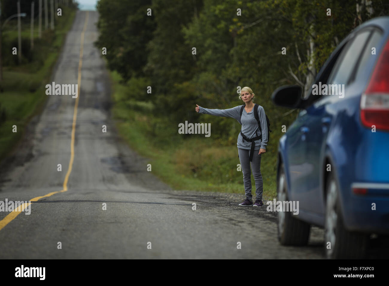 Blonde Woman Hitchhiking On The Side Of The Road And A Car Stopping By