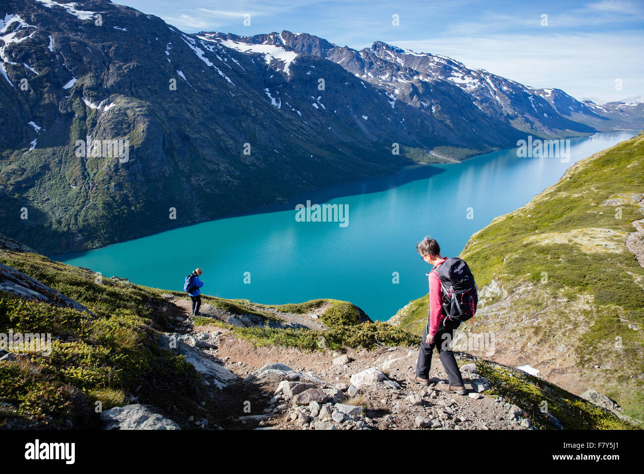 Two walkers above the turquoise waters of Lake Gjende on the Memurubu ...