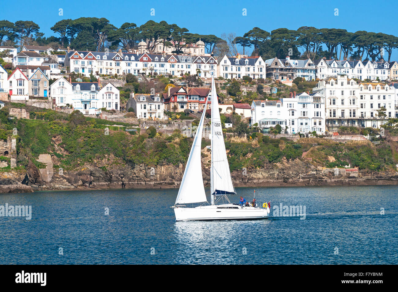A yacht sailing on the river Fowey in Cornwall, UK with the town of ...