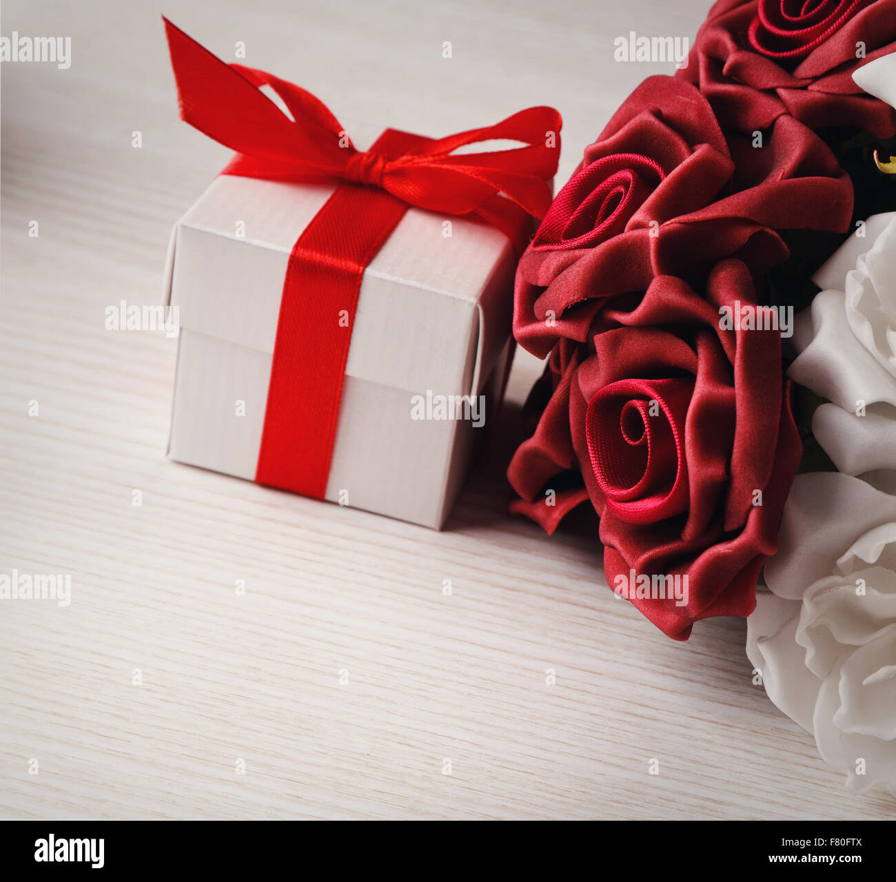 red and white roses and red gift box with yellow ribbon on wooden ...