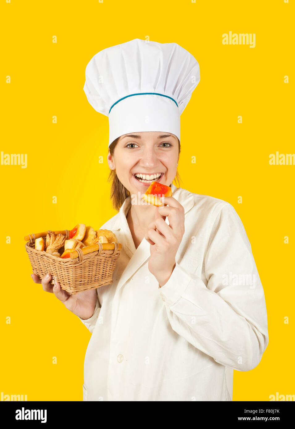 female cook eating tasty pastry over yellow background Stock Photo - Alamy