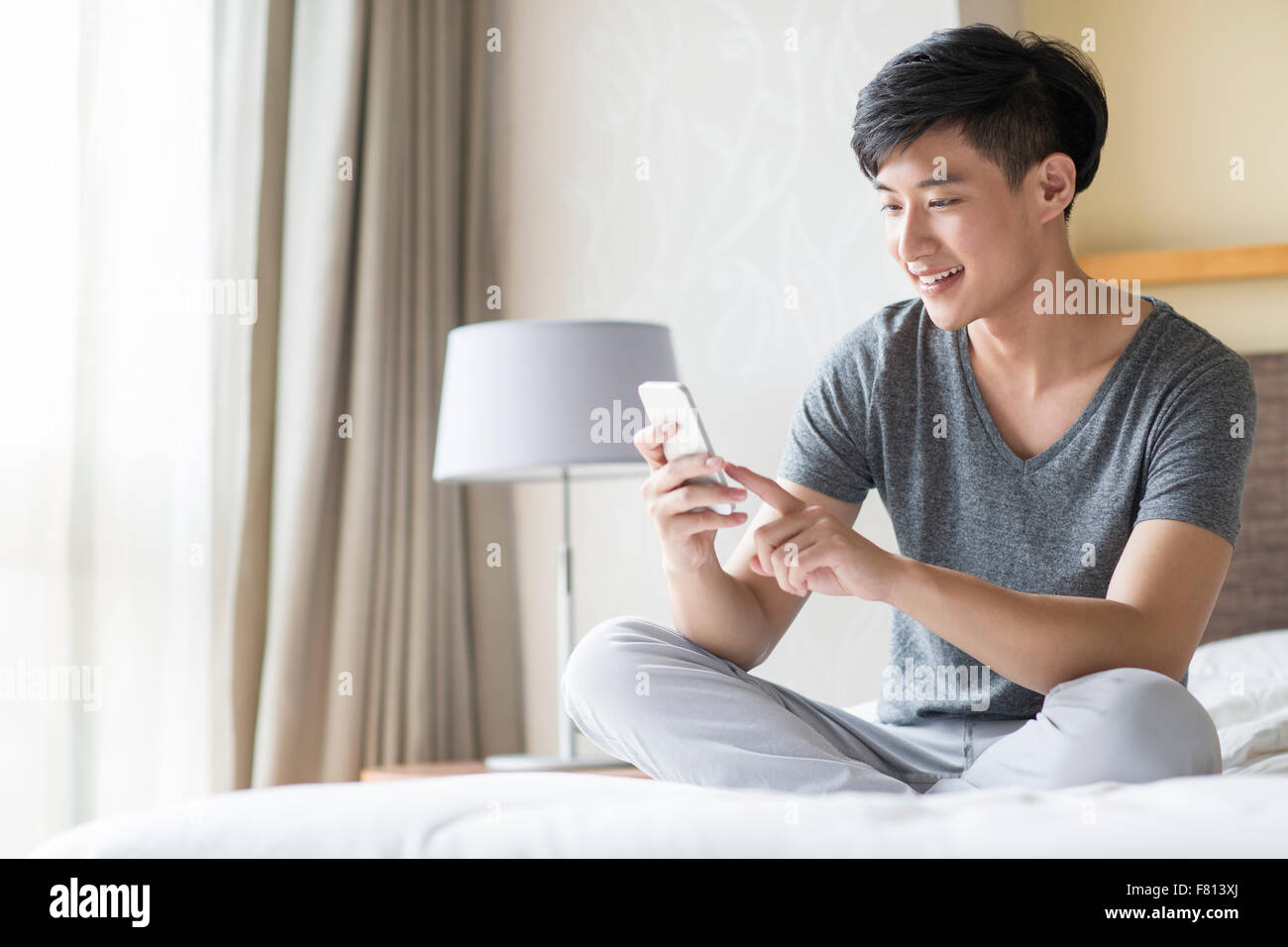 Young man using smart phone on bed Stock Photo - Alamy