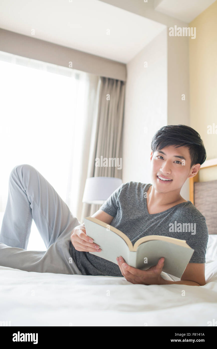 Young man reading book on bed Stock Photo - Alamy