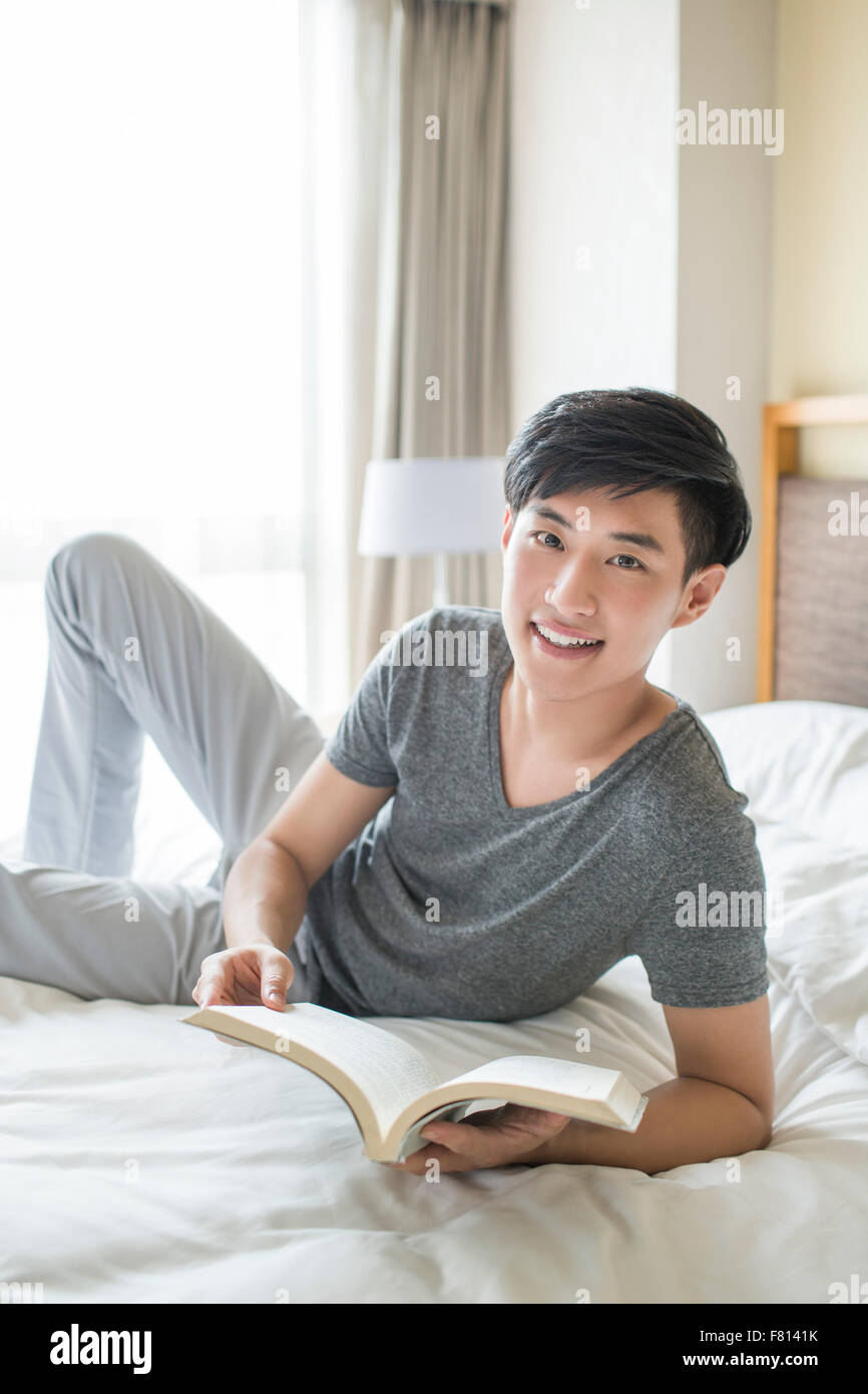 Young man reading book on bed Stock Photo - Alamy