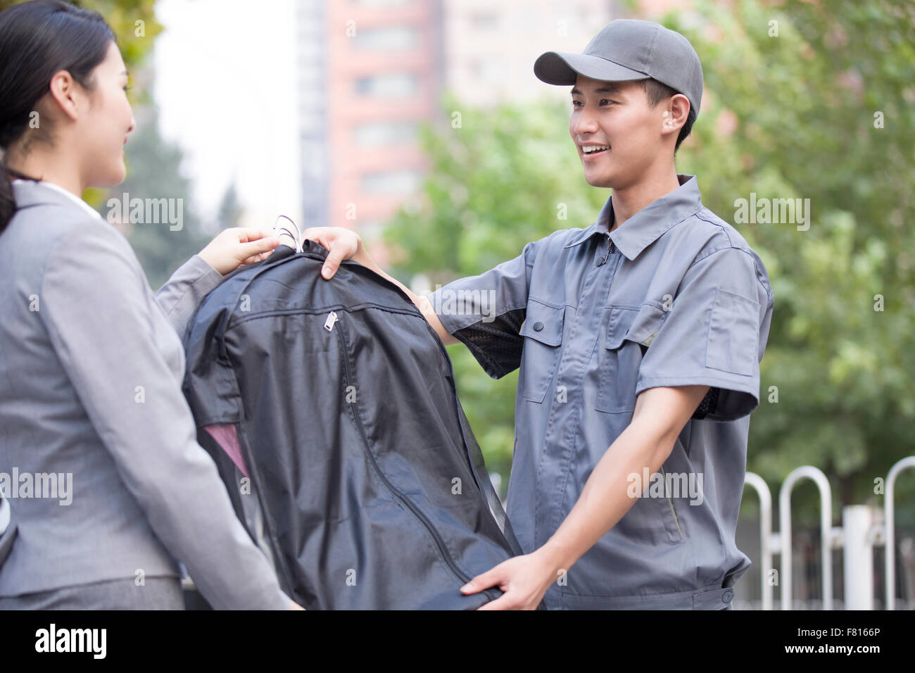 Young woman getting dry-cleaned clothes from delivery person Stock ...
