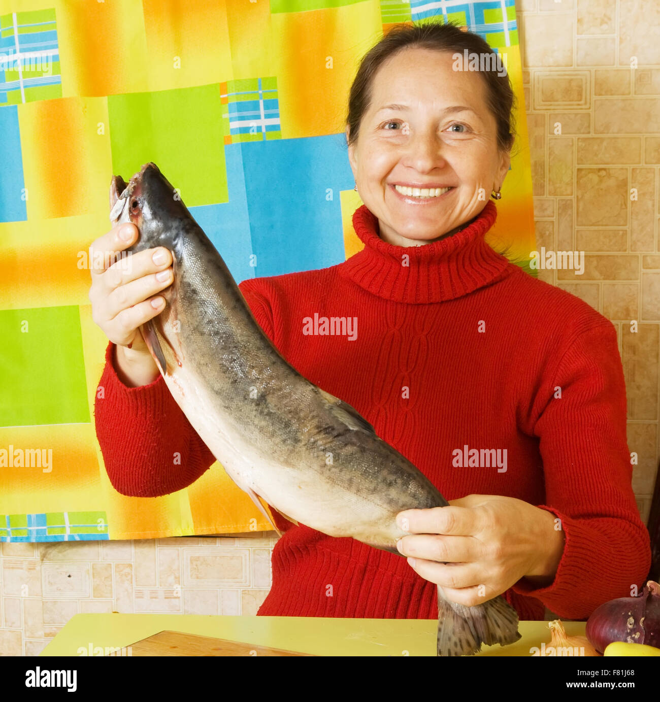 Mature woman with salmon fish in her kitchen Stock Photo - Alamy