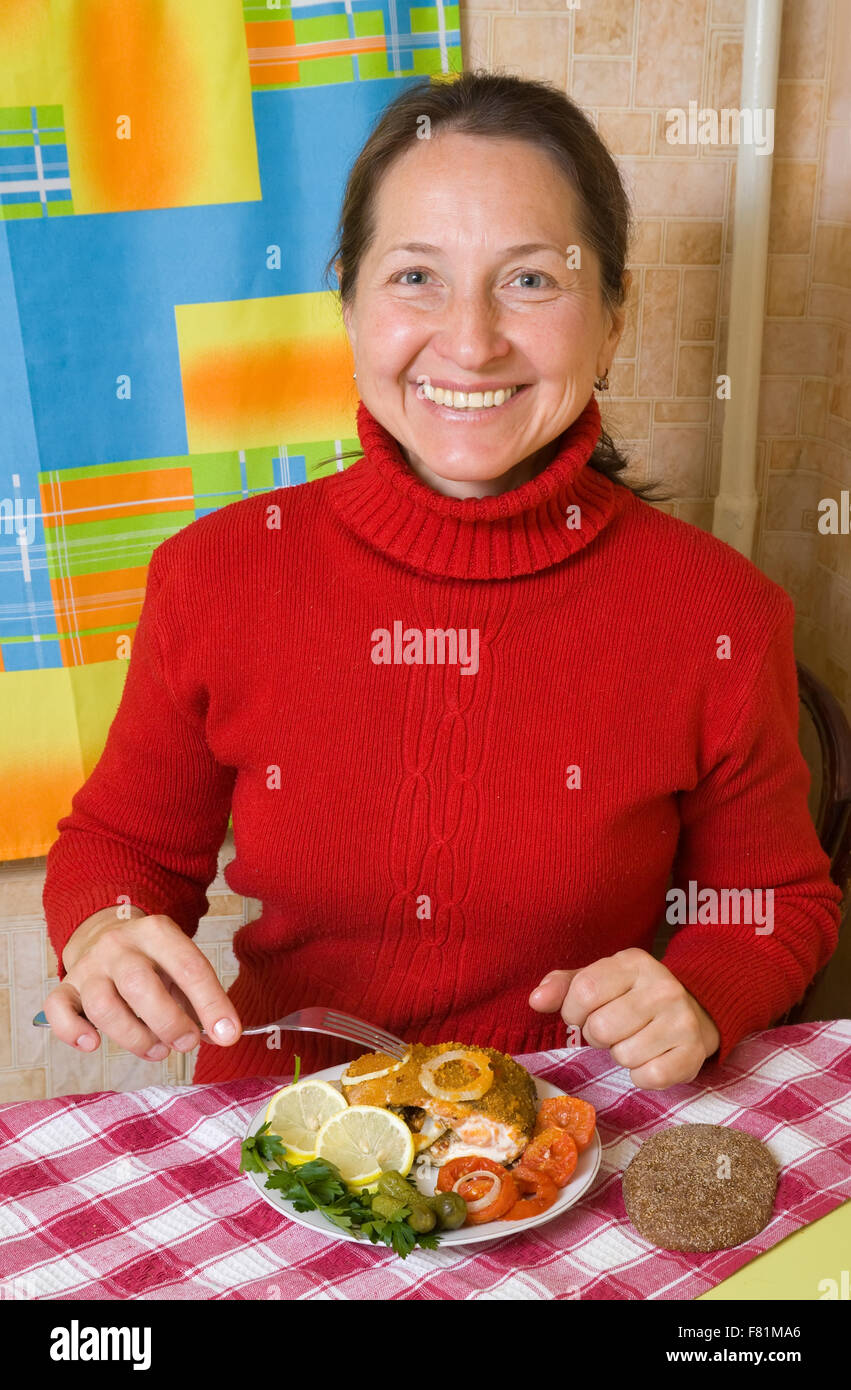 mature woman eating stuffed fish in her kitchen Stock Photo - Alamy
