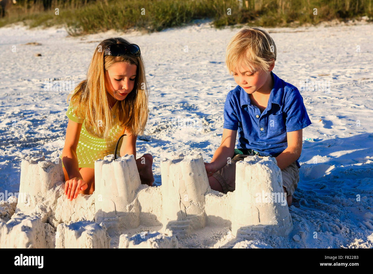 Young Brother And Sister Posing At Sunset By The Sand Castle They Built
