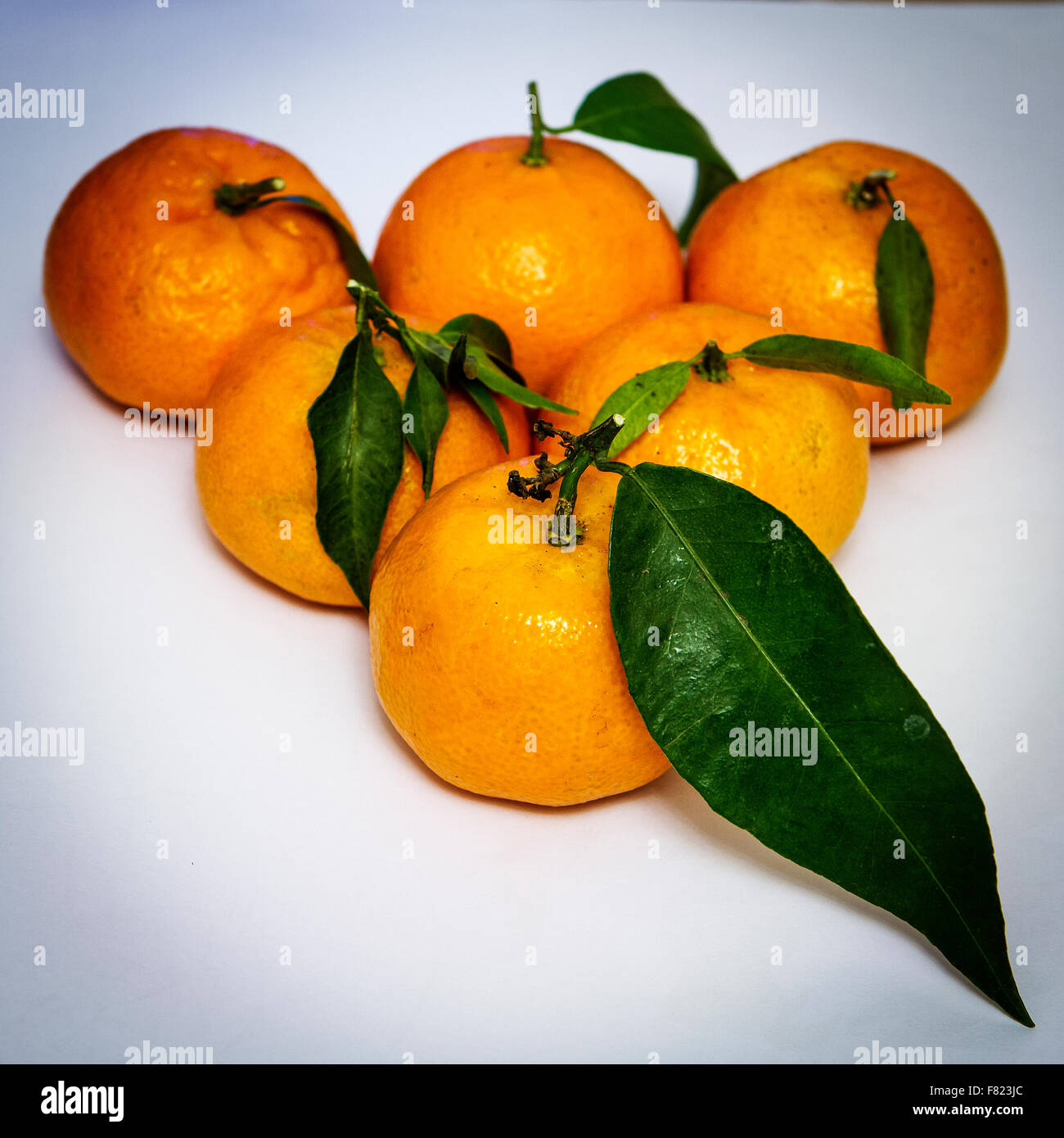 Clementines with their leaves arranged in a triangular shape on a white ...