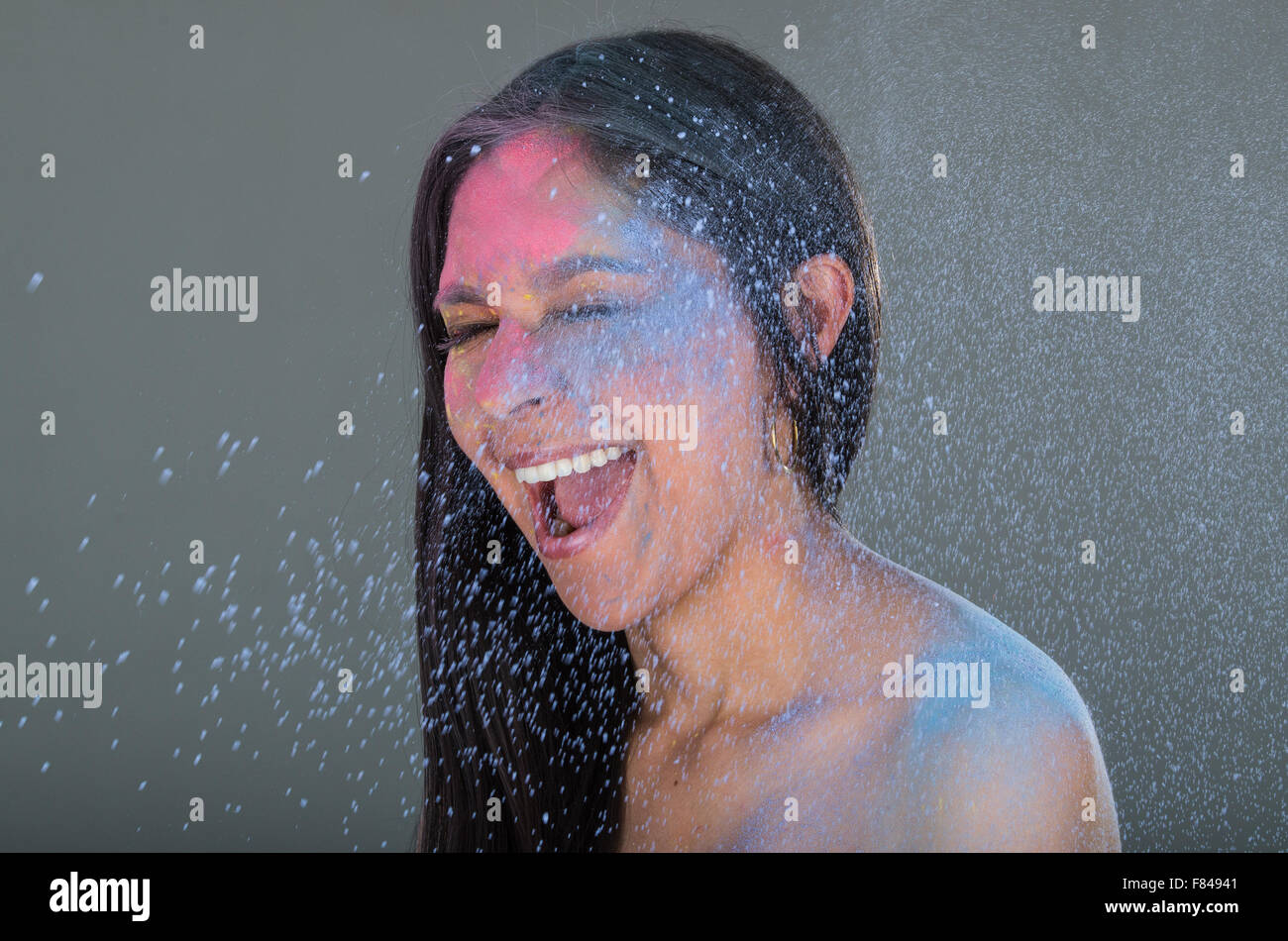 Beautiful young brunette girl with colorful powder blowing in her face ...