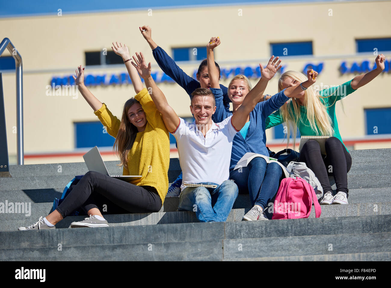 Group portrait of happy students outside in front of school sitting on ...