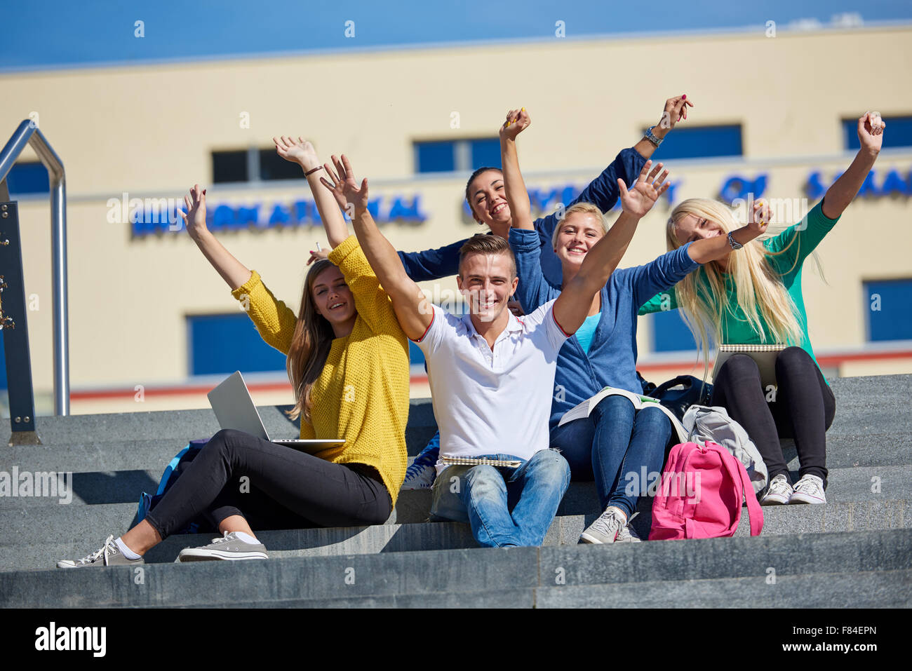 Group portrait of happy students outside in front of school sitting on ...