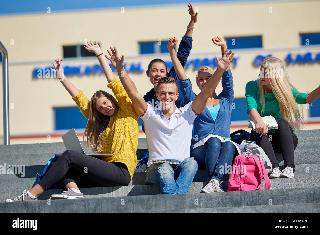 Group portrait of happy students outside in front of school sitting on ...