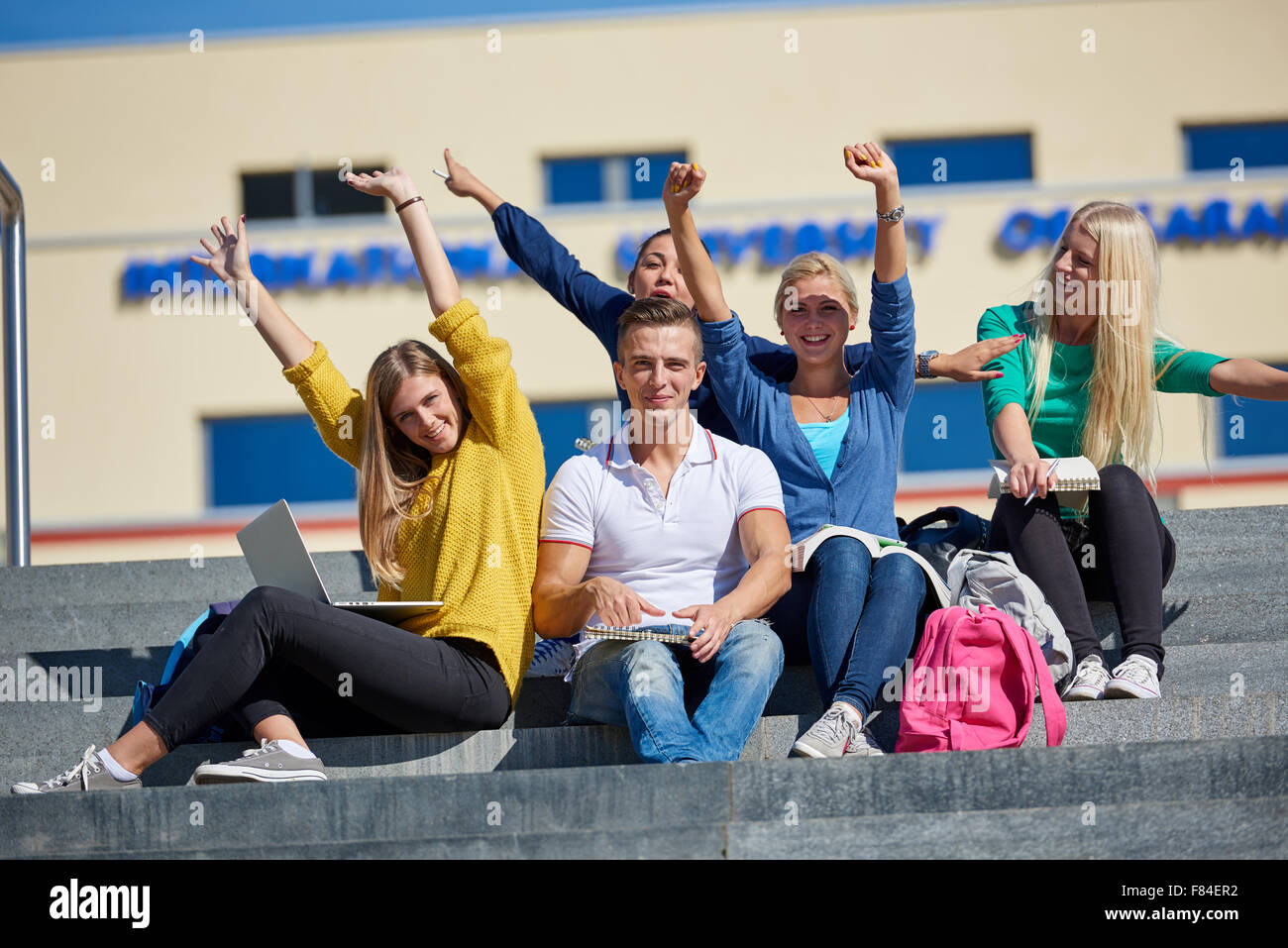 Group portrait of happy students outside in front of school sitting on ...