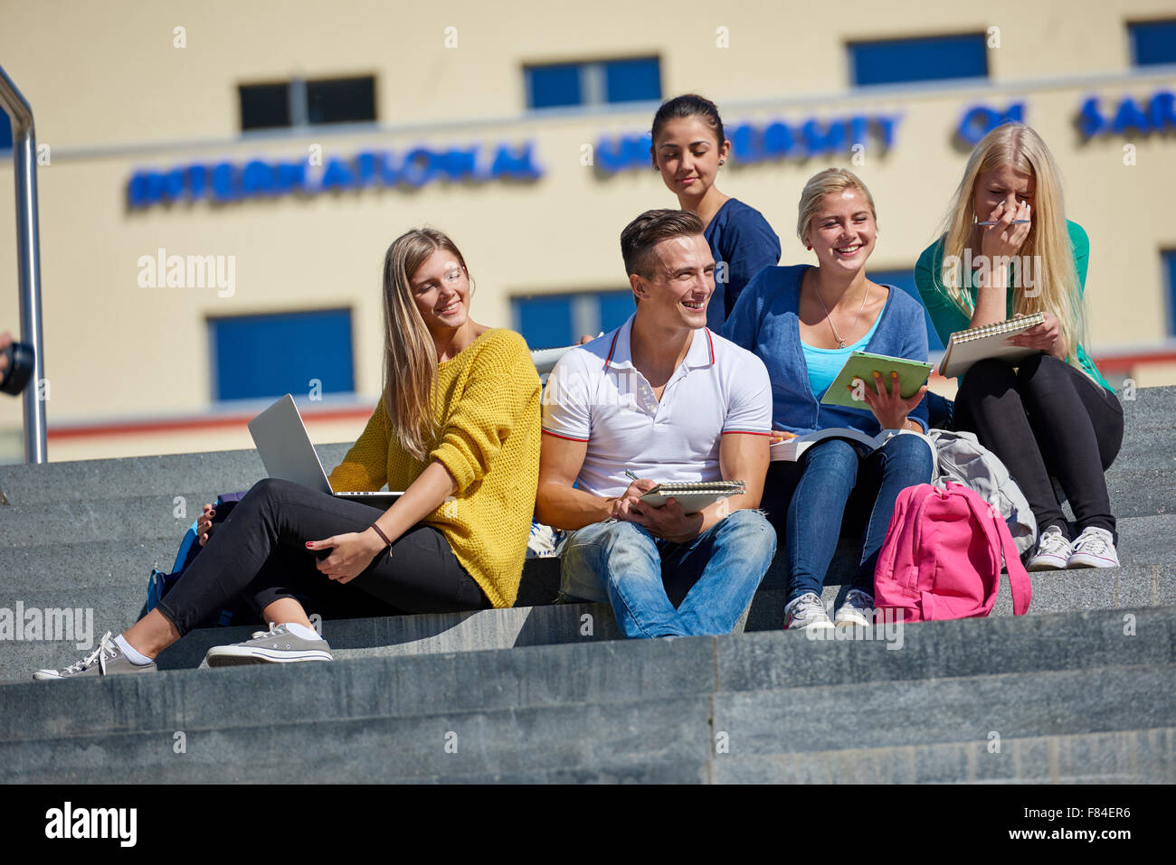 Group portrait of happy students outside in front of school sitting on ...