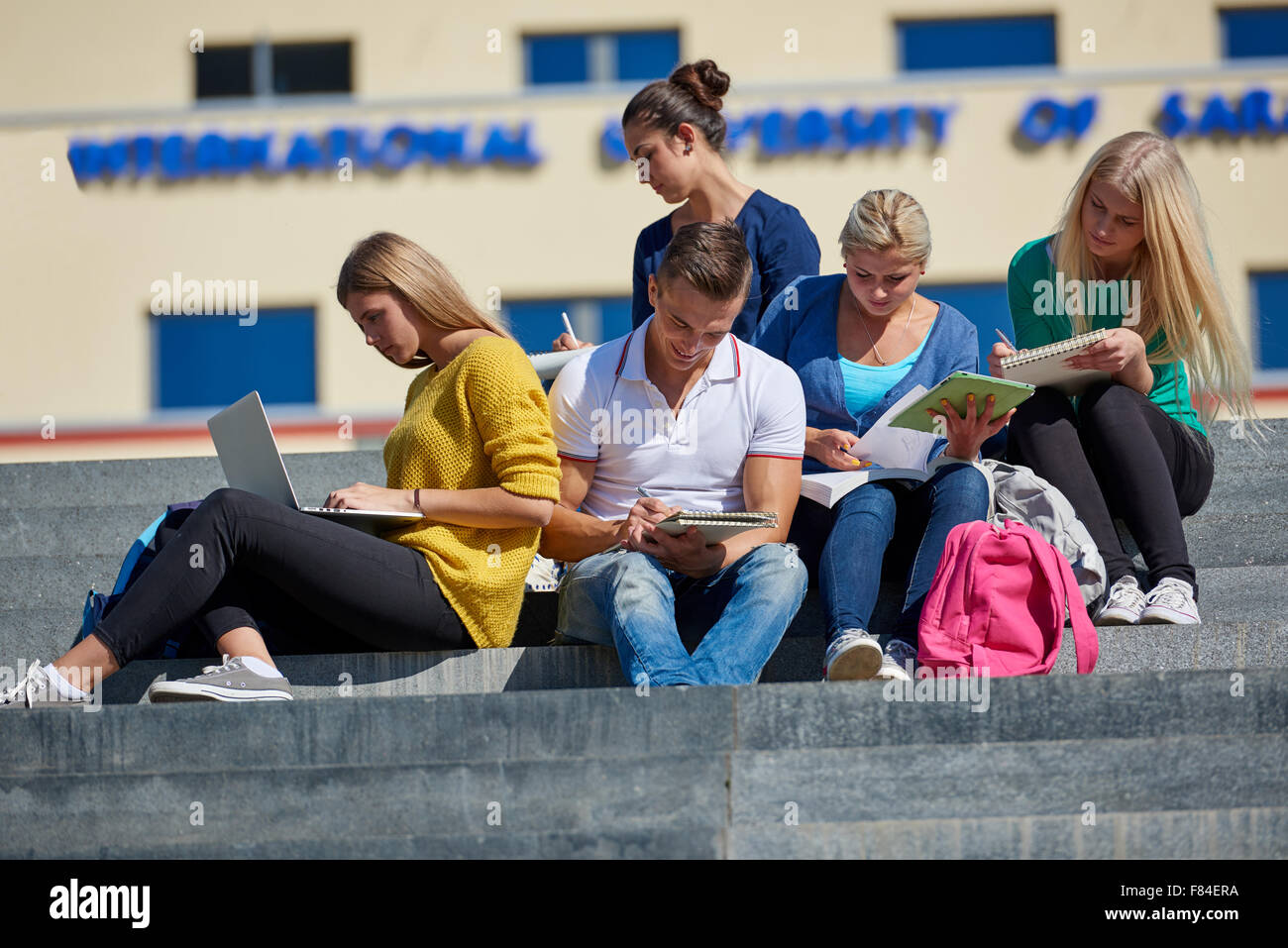 Group portrait of happy students outside in front of school sitting on ...