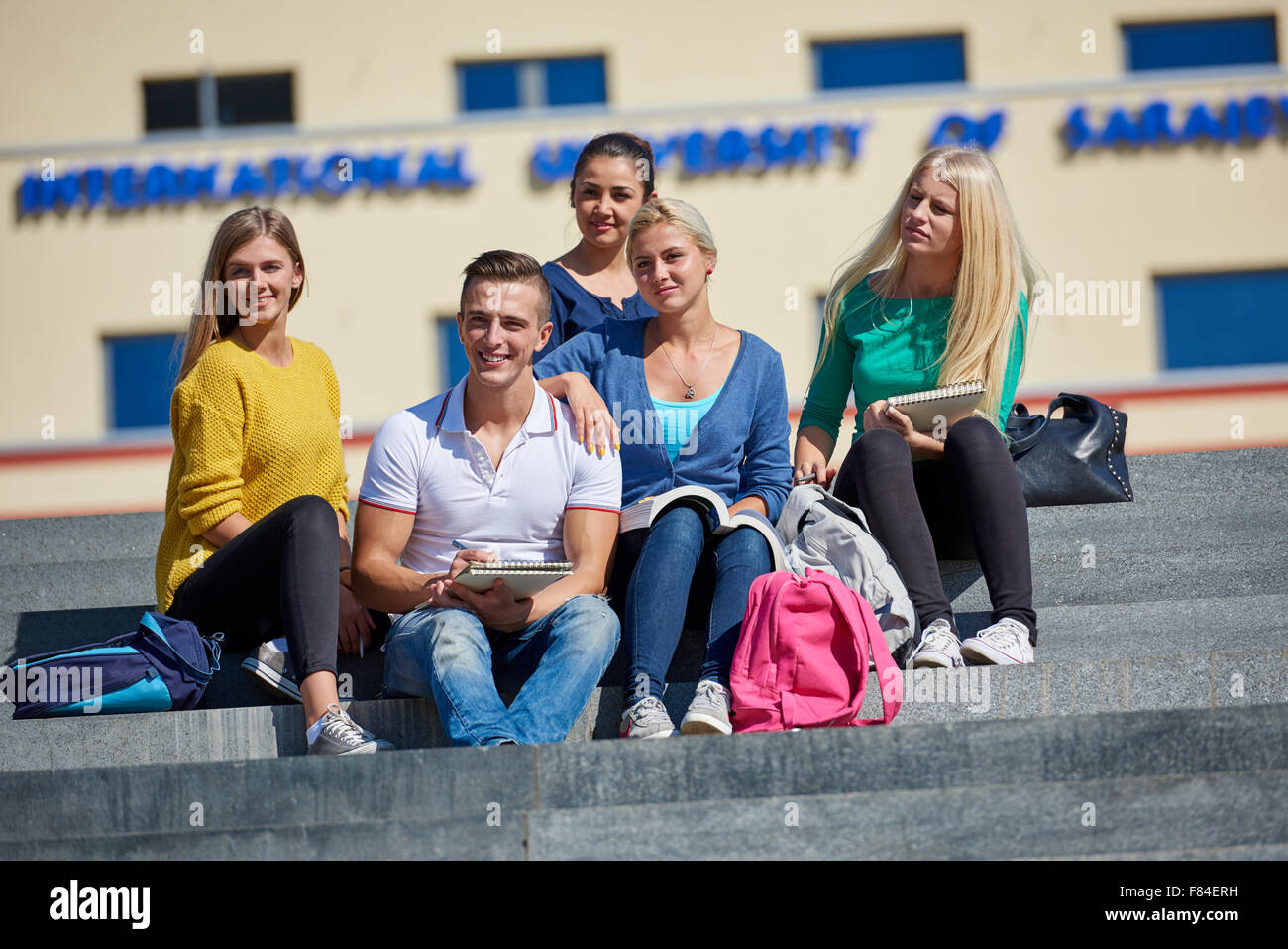 Group portrait of happy students outside in front of school sitting on ...