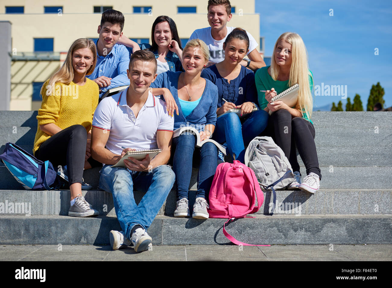 Group portrait of happy students outside in front of school sitting on ...