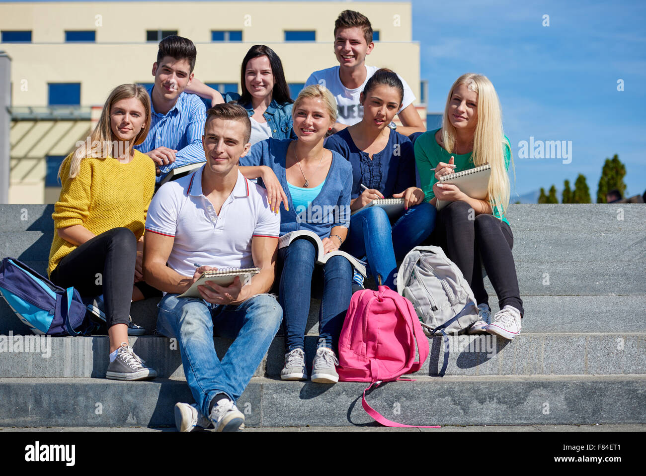 Group portrait of happy students outside in front of school sitting on ...
