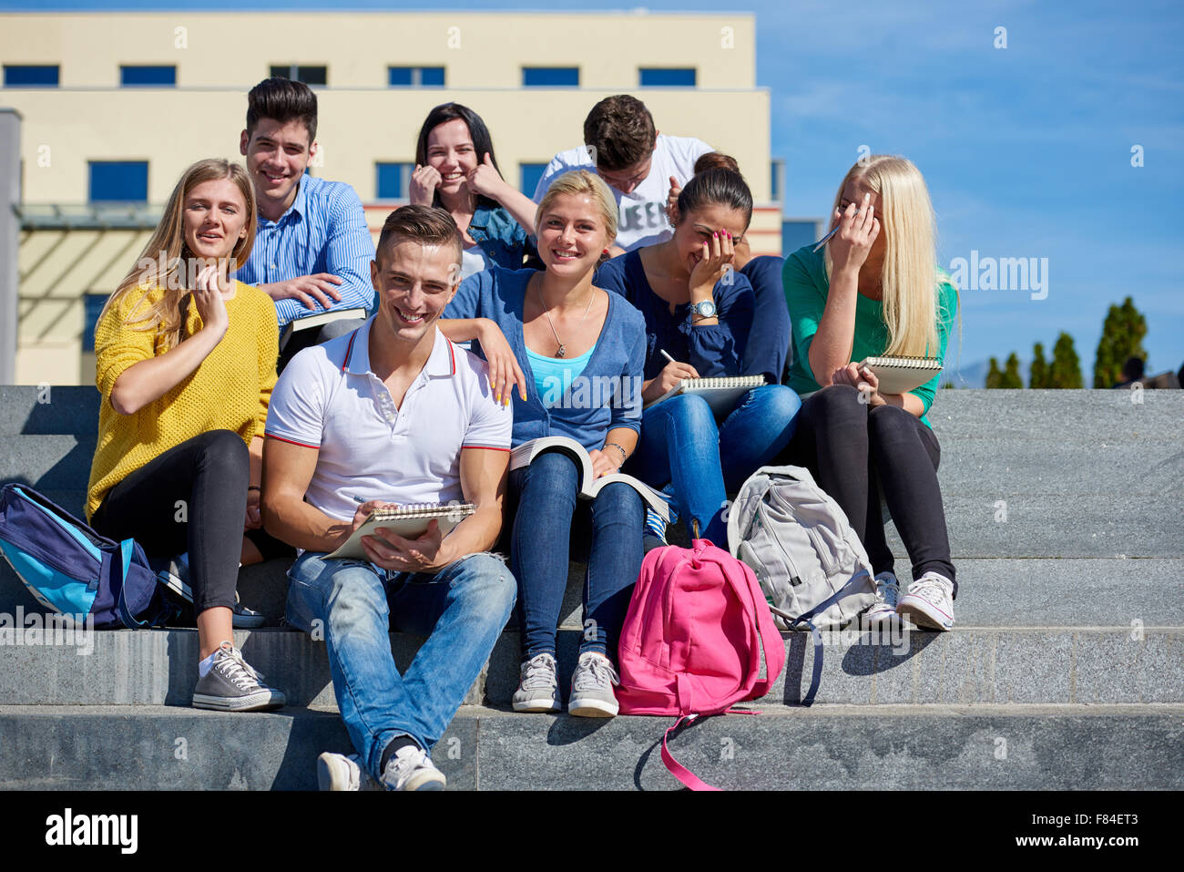Group portrait of happy students outside in front of school sitting on ...