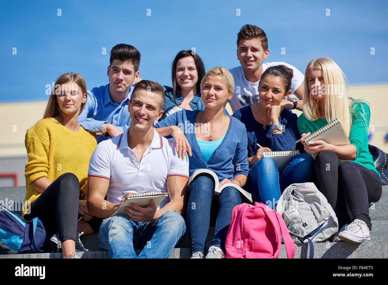 Group portrait of happy students outside in front of school sitting on ...