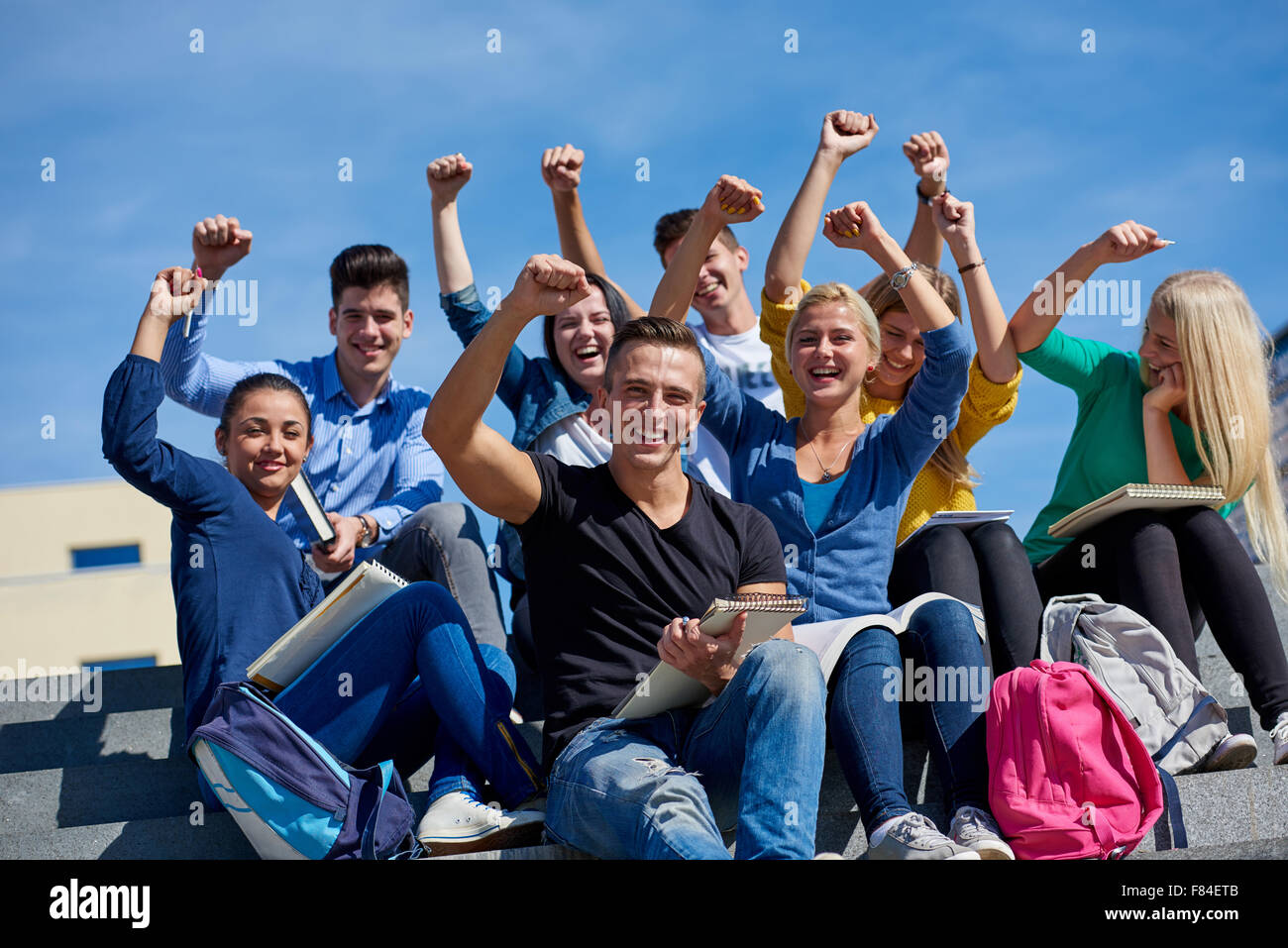 Group portrait of happy students outside in front of school sitting on ...