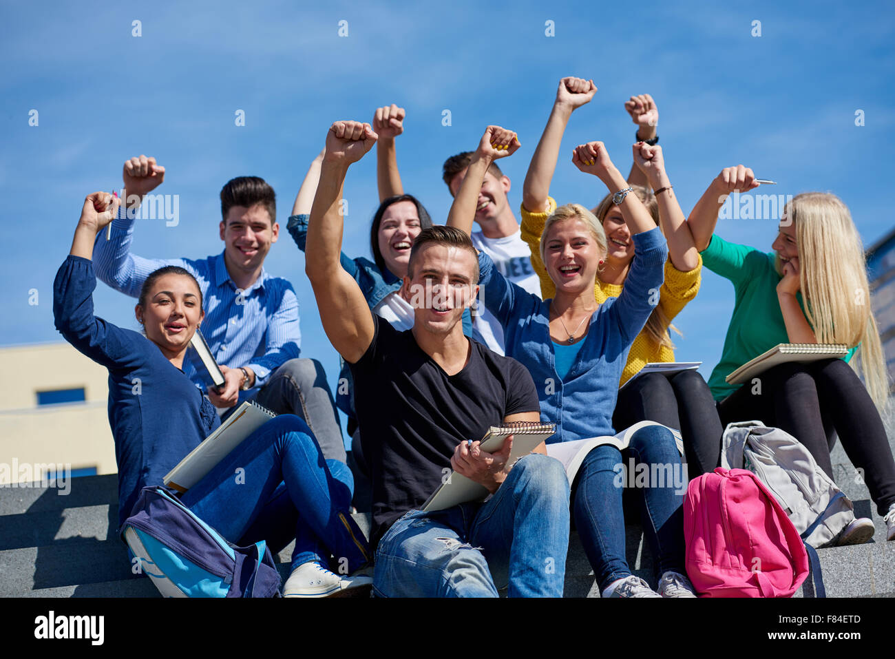 Group portrait of happy students outside in front of school sitting on ...